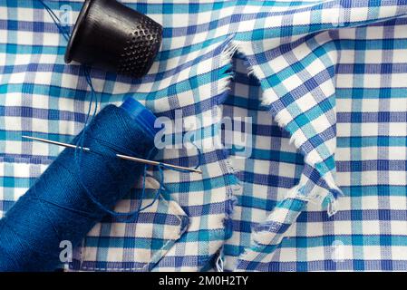 A needle and thread lies on torn or holey clothes. Shirt with a hole ...
