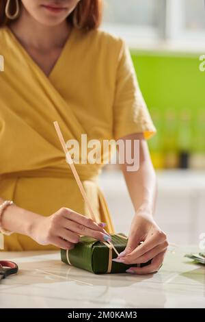 Closeup image of woman packing square cake she made in banana leaves ...