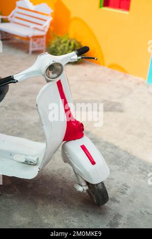 A Vertical shot of a white Vespa scooter in the street with trees in ...
