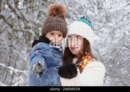 Mom and son are walking and light sparklers in the snow winter forest ...