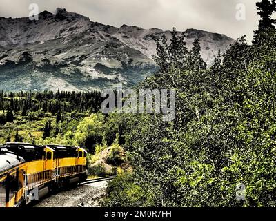 Alaska - Yellow train rounding a curve, going downhill in the mountains ...