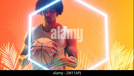 Biracial basketball player with afro hair holding ball by illuminated ...