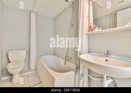 Flush toilet located between sink and shower in small tiled bathroom of ...