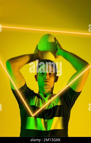 Portrait of caucasian male rugby player holding ball by illuminated ...