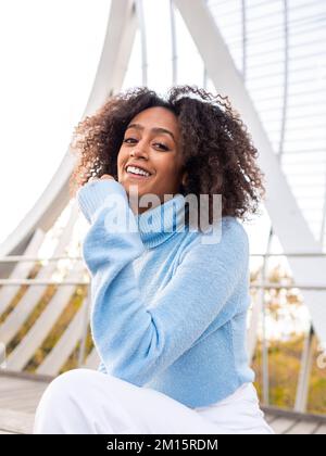 From below of cheerful young dreamy Hispanic female in warm sweater ...