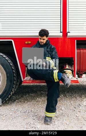Focused Hispanic firefighter in uniform sitting on step outside fire ...