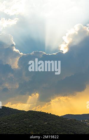 A beautiful shot of the sun shining behind the mountains under a cloudy ...