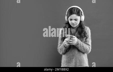busy teen girl in sweater in headphones for listening music texting in ...