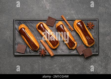 Board with delicious eclairs, cinnamon and chocolate on dark background ...