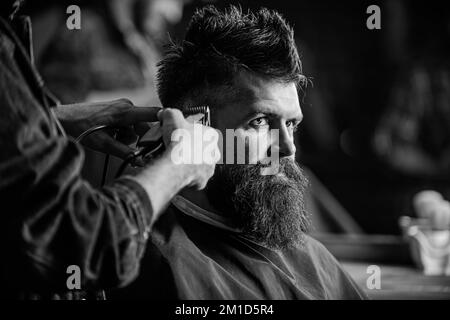 Barber works with a beard clipper. Hipster client getting haircut Stock ...