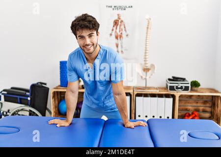 Young hispanic man wearing physio therapist uniform using touchpad at ...