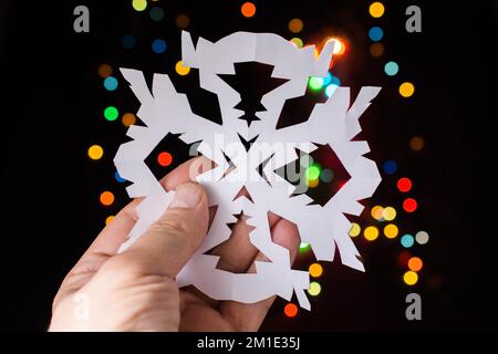 Snowflake shaped paper in hand on bokeh light background Stock Photo - Alamy