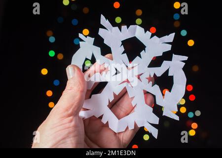 Snowflake shaped paper in hand on bokeh light background Stock Photo - Alamy