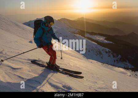 Skier freerider starts descent, beautiful sunset of golden sun and ...