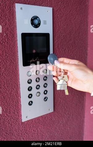 A young woman types the apartment code on the electronic intercom panel ...