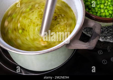 Stick blender blends pea soup in pot on hob, pea on strainer, closeup ...