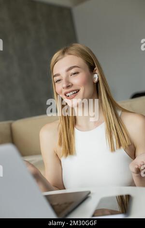 Blonde coach in wireless earphone talking during video call on laptop ...