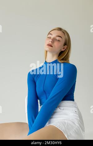 blonde woman in blue zipped turtleneck sitting with closed eyes and ...