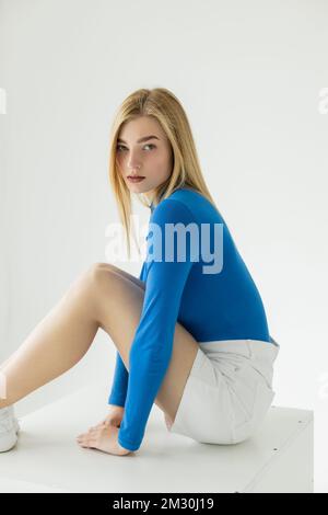 pretty woman in blue turtleneck and white shorts sitting in black ...