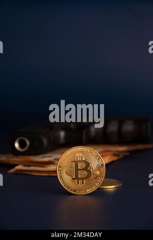 Bitcoin coin in the foreground with a gun and euros, defocused in the ...