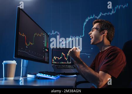 Side view of male crypto broker sitting at his workplace at night, blue ...