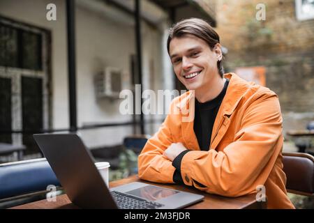 Freelancer in jacket looking at laptop near cup on couch in living room ...