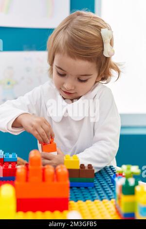 Adorable caucasian girl playing with construction blocks sitting on ...