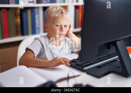 Adorable toddler student boring using computer sitting on table at ...