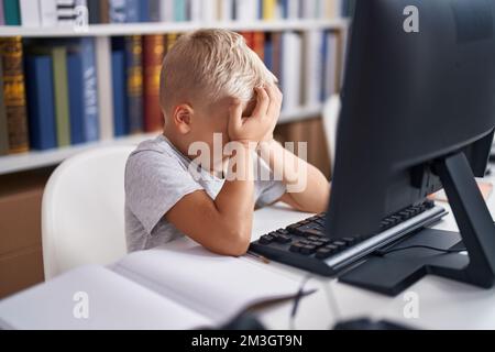 Adorable toddler student boring using computer sitting on table at ...