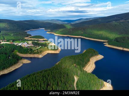An aerial shot of Oasa lake in Romania surrounded by fir forest trees ...