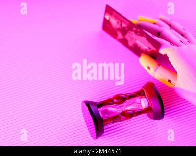 Bank card in an artificial hand. Credit card and hourglass in neon ...