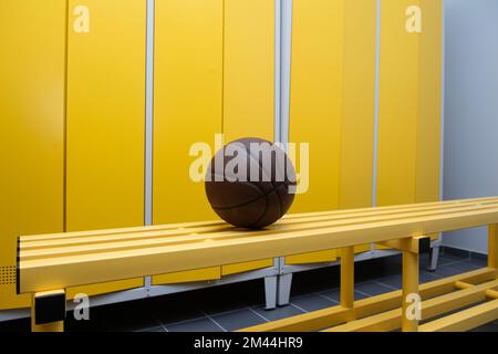 Brown basketball ball on yellow bench in locker room. Horizontal sport ...