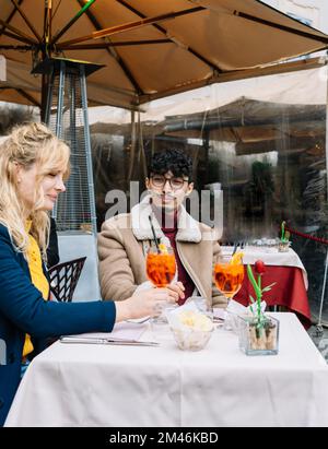 Young multi-ethnic engaged couple having drinks on a sunny fall/winter ...
