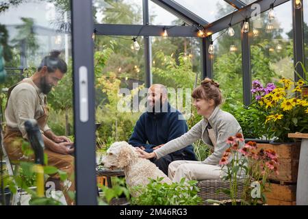Smiling friends sitting in greenhouse Stock Photo - Alamy