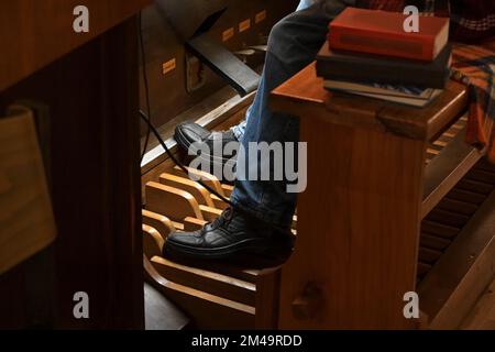 Foot of an organist is playing on the pedal board of a pipe organ in a ...