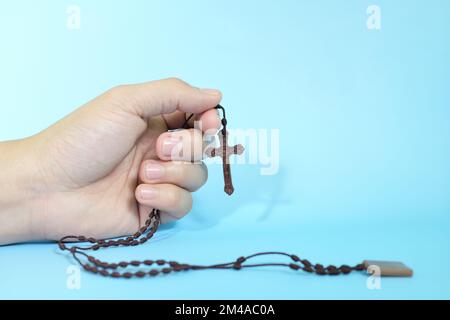 Human hand praying and holding a scapular rosary in blue background ...