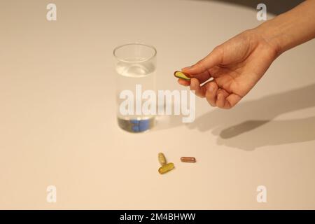 Woman is taking medicine with cup of water on the white table, girl is ...