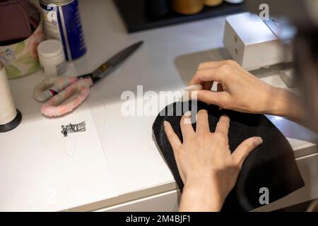 Woman is sewing black beanie hat on a sewing machine, using a sewing ...