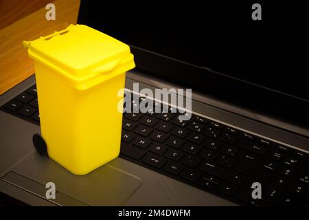 A miniature yellow bin on a laptop representing electronic waste ...