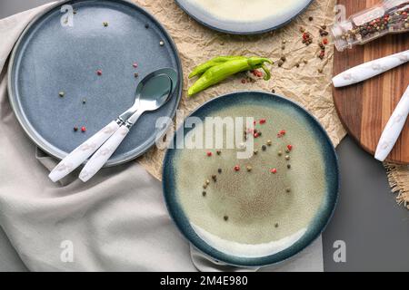 Composition with plates, peppercorns and spoons on grey background ...