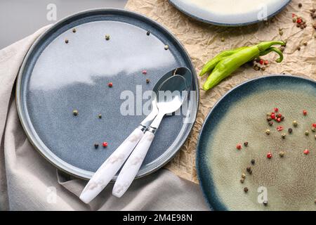 Composition with plates, peppercorns and spoons on grey background ...