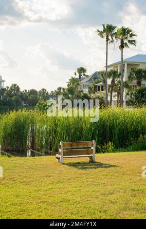 Small bench facing the tall grasses in the lake at the front of houses ...