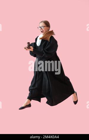 Angry female judge with gavel jumping on pink background Stock Photo ...