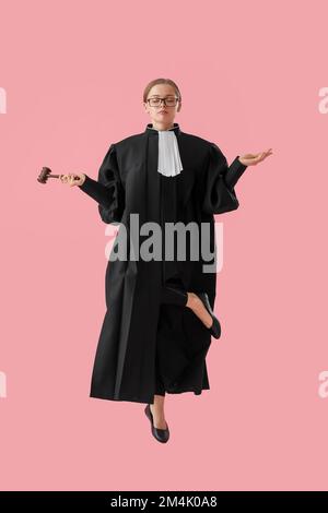 Young female judge with gavel jumping on pink background Stock Photo ...