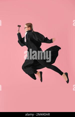 Young female judge with gavel jumping on pink background Stock Photo ...