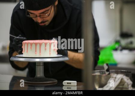 cake chef designer preparing a pink dripping on white frosted cake for ...
