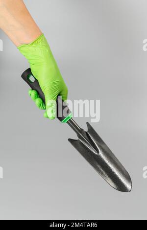 Small garden trowel in a hand dressed in a glove on gray background ...
