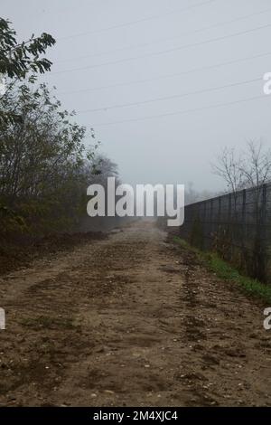 Dirt path bordered by a metallic fence on a foggy day Stock Photo - Alamy