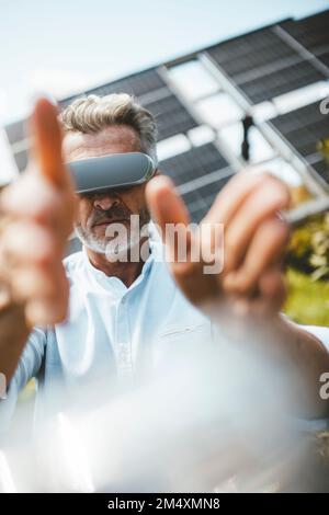 Mature man gesturing with futuristic glasses in front of solar panels ...