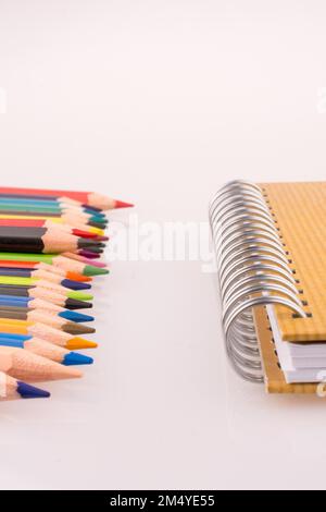 Color pencils of various colors near a notebook on a white background ...